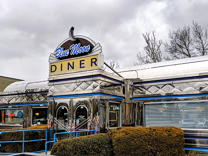 The iconic Blue Moon Diner sign shines like a beacon for hungry travelers, promising classic American comfort in its gleaming chrome exterior.