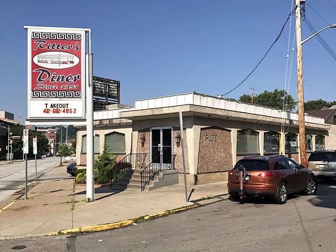 The iconic red sign beckons like a lighthouse for hungry souls. Ritter's Diner's mid-century exterior promises comfort food salvation at any hour.