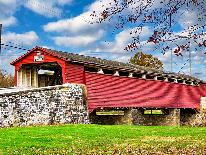 Like a postcard from Pennsylvania's past, the vibrant red exterior of Wehr Bridge stands proudly against blue skies, its weathered stone foundations anchoring history to the present.