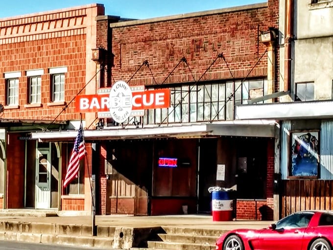The brick façade of Louie Mueller Barbecue stands as a humble temple to Texas' most sacred culinary tradition, complete with an American flag that says "patriotism tastes delicious."