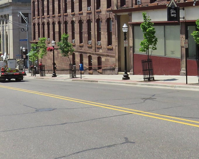 Downtown Marquette stretches invitingly toward the hills beyond, its flower-adorned lampposts and historic buildings creating a postcard-perfect main street scene.