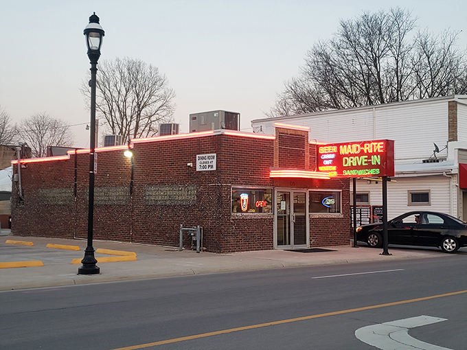 The neon glow of Maid-Rite's vintage sign beckons like a lighthouse for hungry travelers, promising simple pleasures in a brick-wrapped package.