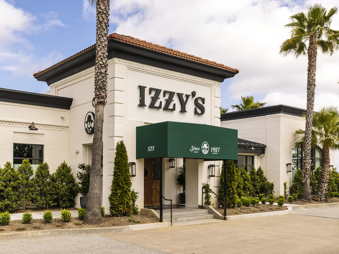 The iconic white exterior of Izzy's on the Peninsula stands like a beacon for carnivores, palm trees swaying as if applauding your excellent dinner choice.