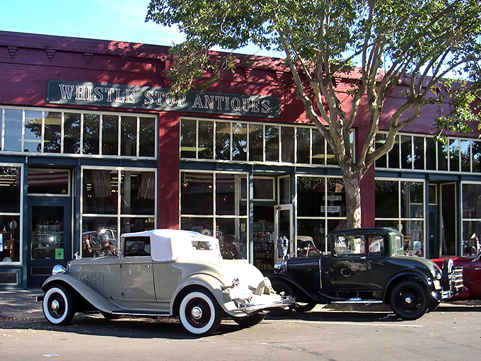 The crimson facade of Whistlestop Antiques stands proudly alongside vintage automobiles that look ready for a Gatsby-era joyride. Time travel begins at the curb.