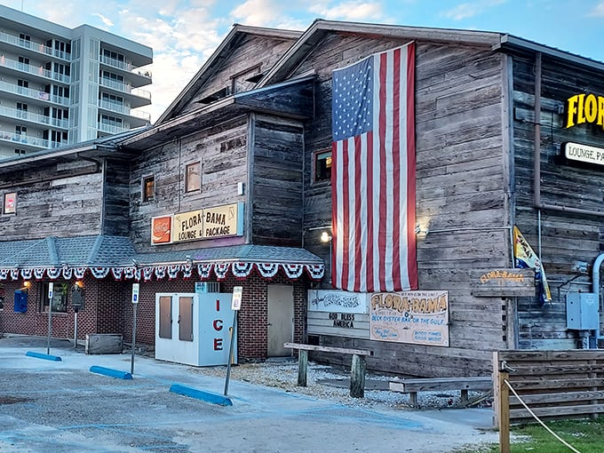 The weathered wooden exterior of Flora-Bama proudly displays its iconic yellow signage and American flag &ndash; a true Gulf Coast landmark straddling two states.