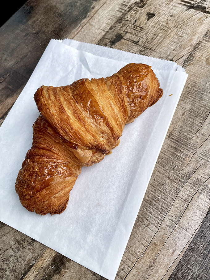 Croissant perfection captured mid-bite&mdash;the honeyed exterior shatters to reveal those distinct, airy layers within.