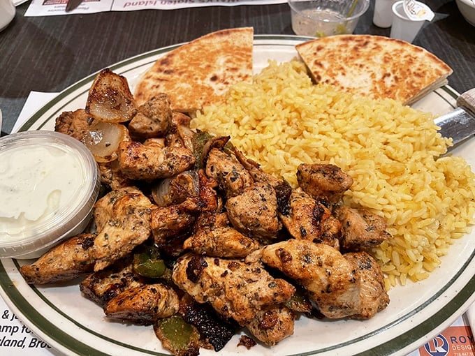 Greek influence shines in this souvlaki platter—tender chicken, sunny yellow rice, and warm pita create a Mediterranean vacation on a classic diner plate.