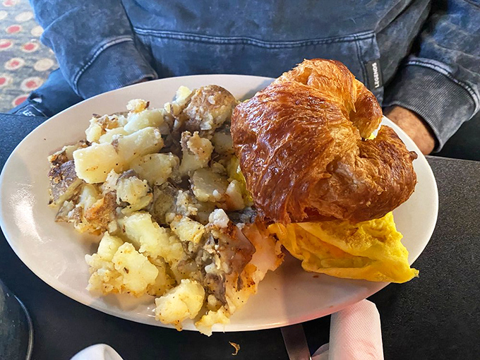 A breakfast sandwich on a buttery croissant with golden home fries&mdash;proof that mornings can indeed be wonderful.