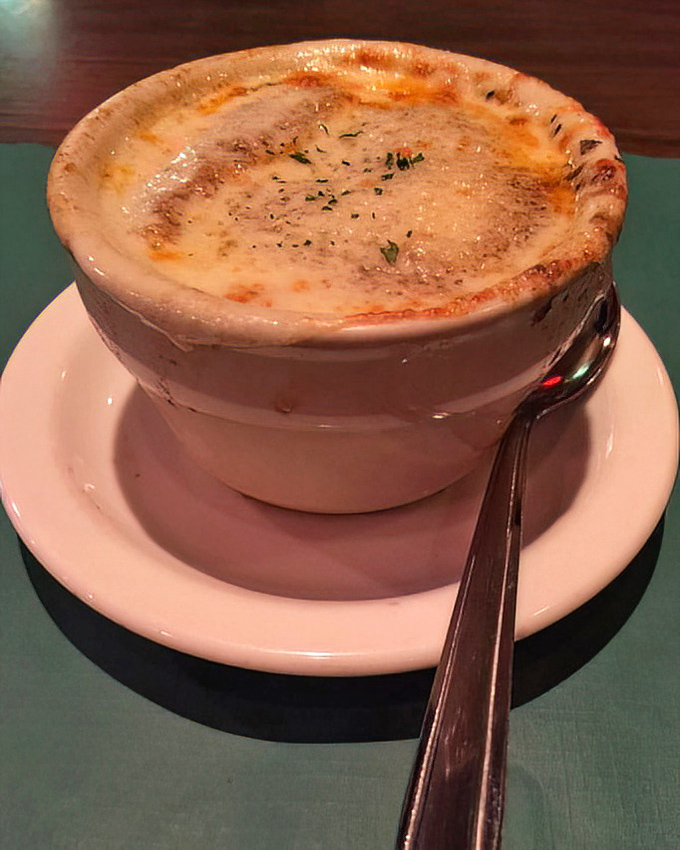 The French onion soup arrives like a sealed treasure chest &ndash; that golden, bubbling cheese top hiding the savory broth and tender onions below.