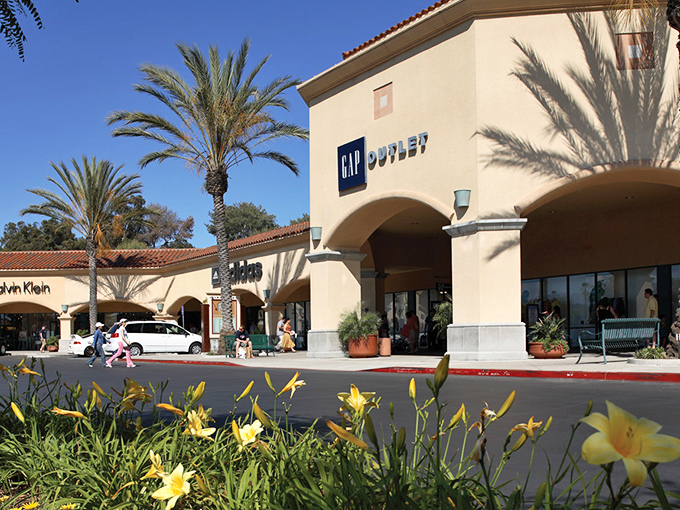 Gap Outlet's sunny storefront, flanked by golden daylilies, offers timeless American classics at prices that won't send your budget into therapy.