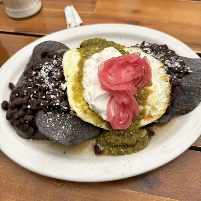 Black bean tortillas cradle a sunny-side egg crowned with salsa verde and pickled onions &ndash; breakfast reimagined with artistic flair.