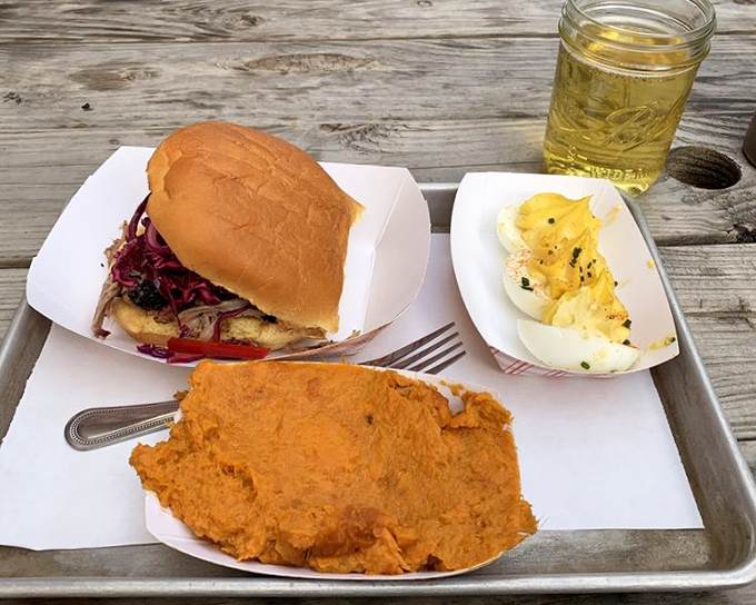 A sandwich that requires both hands and your full attention – pulled pork topped with vibrant slaw on a soft bun, served with deviled eggs and sweet potato mash.