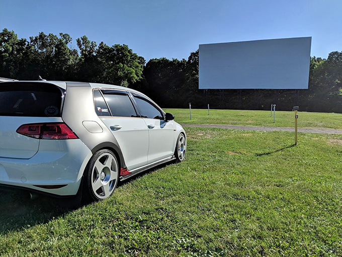 A modern car faces the timeless pleasure of outdoor cinema, two technologies from different eras meeting in perfect harmony.