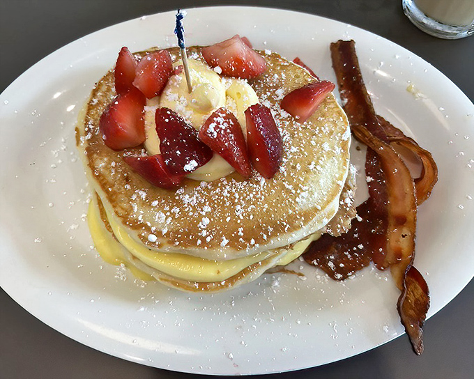 Pancakes wearing strawberries like they're fancy jewelry. The bacon on the side is just there to remind you this is still technically breakfast, not dessert.
