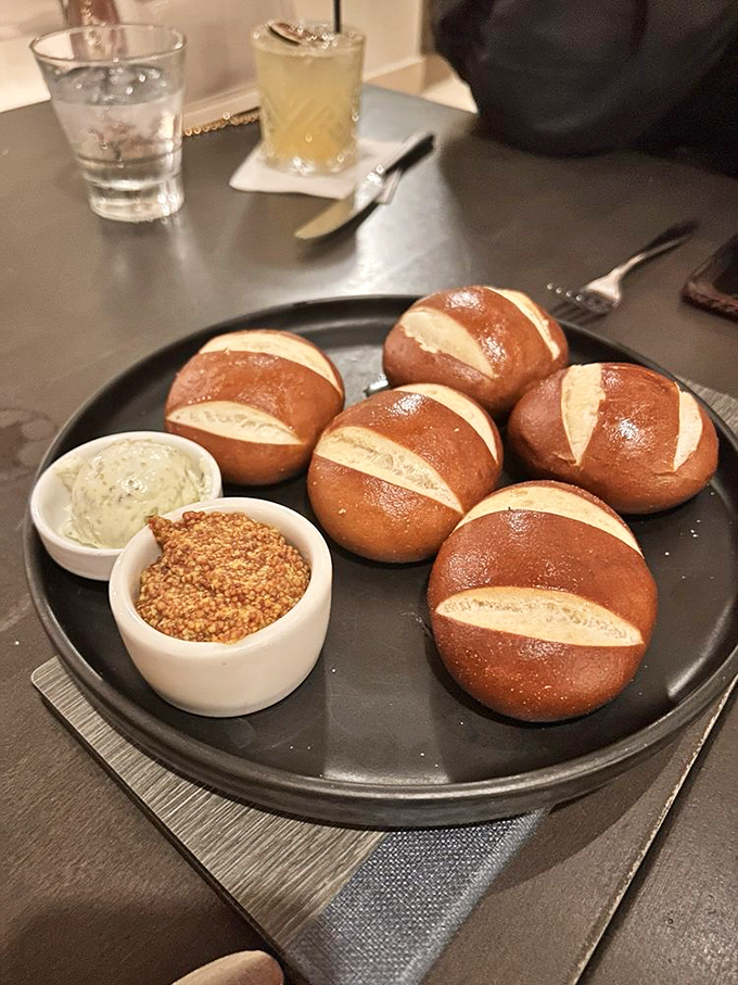 Pretzel rolls that would make a Bavarian proud—served warm with mustard and herb butter that transforms bread service from obligation to obsession.