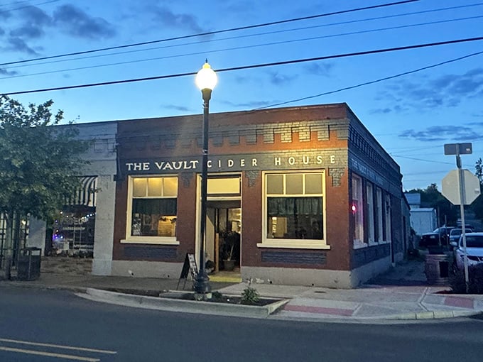As twilight falls, The Vault Cider House glows with invitation, transforming a historic brick building into the town's evening gathering spot.