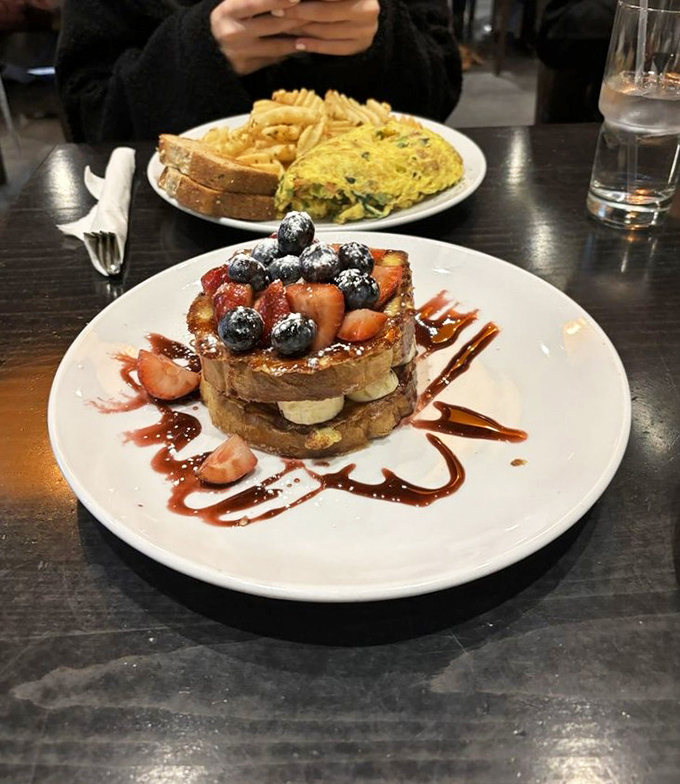 Stuffed French toast that looks like it escaped from a dessert menu, crowned with fresh berries and artistic drizzles of sweet sauce.