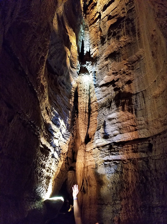 A visitor reaches toward the heavens in this narrow passage. In caves, the journey upward is as breathtaking as the journey downward.