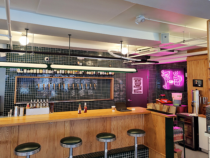 The bar area glows with neon promise, where wooden stools await patrons seeking libations to complement their culinary adventures.