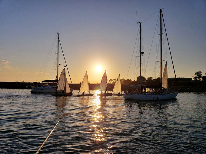 Sailboats dance their way back to harbor at sunset, creating a ballet of masts and sails with the lighthouse as their audience. 