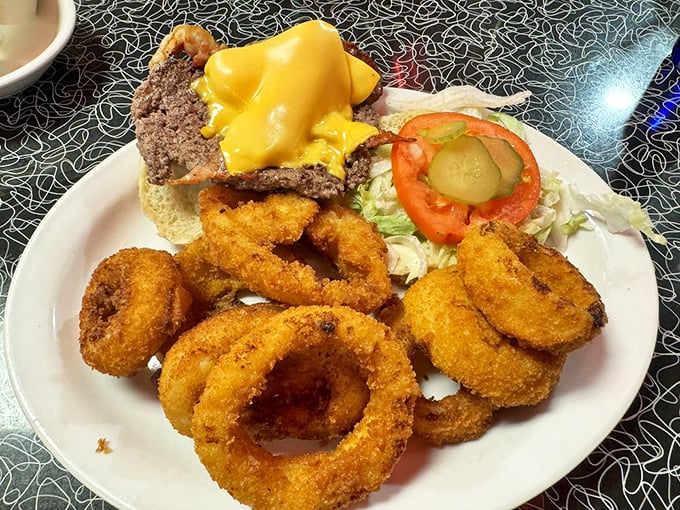 A burger that requires both hands and a strategy, flanked by onion rings that crunch loud enough to turn heads.
