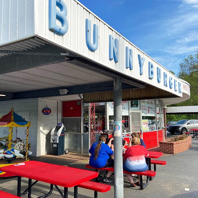 The BUNNYBURGER sign looms like a beacon of hope for hungry travelers. Those red picnic tables below? Front-row seats to culinary nostalgia.