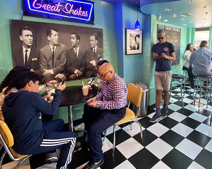 Milkshake pilgrims at the altar of deliciousness. Visitors enjoy their frozen treasures beneath vintage photographs in this shrine to sweet satisfaction.