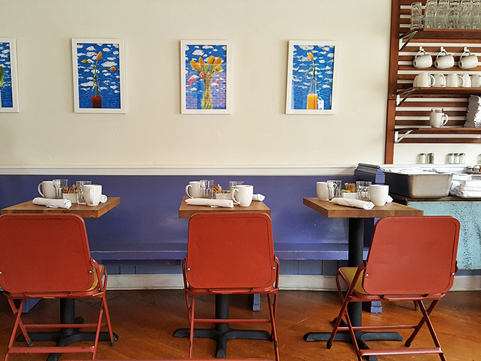 Bright artwork against blue wainscoting creates the perfect backdrop for these coral chairs &ndash; like a Wes Anderson film set where the food actually tastes good.