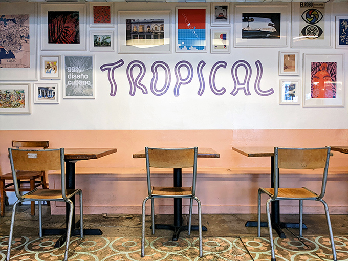 The wall of framed art creates a gallery-like backdrop for simple wooden chairs, where conversations flow as freely as the coffee.