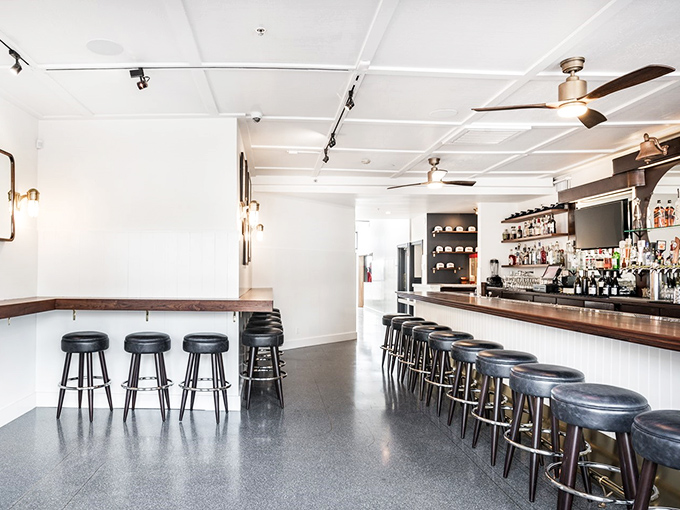 The bar area's sleek minimalism says "we're serious about drinks" while the stools patiently await your stories.