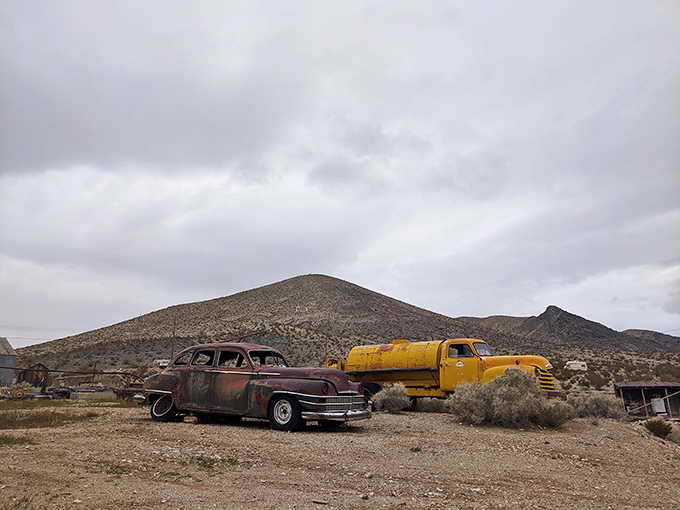 A vintage car and yellow truck stand sentinel against the mountain backdrop&mdash;desert sculptures with stories to tell.