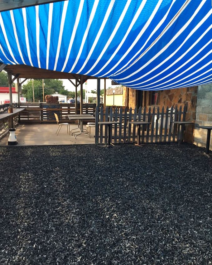 The outdoor seating area offers a blue-striped canopy that feels like dining under an Oklahoma sky, minus the tornado warnings.