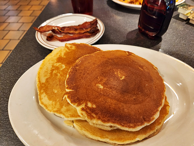 Pancakes so perfectly golden they belong in Fort Knox, with a slice of bacon standing guard against anyone who might try to steal a bite.