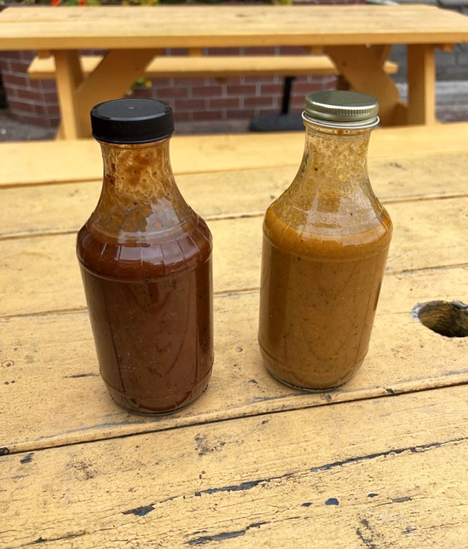 Two bottles of house-made sauce sitting pretty on a wooden table&mdash;one sweet, one tangy, both essential to the experience.