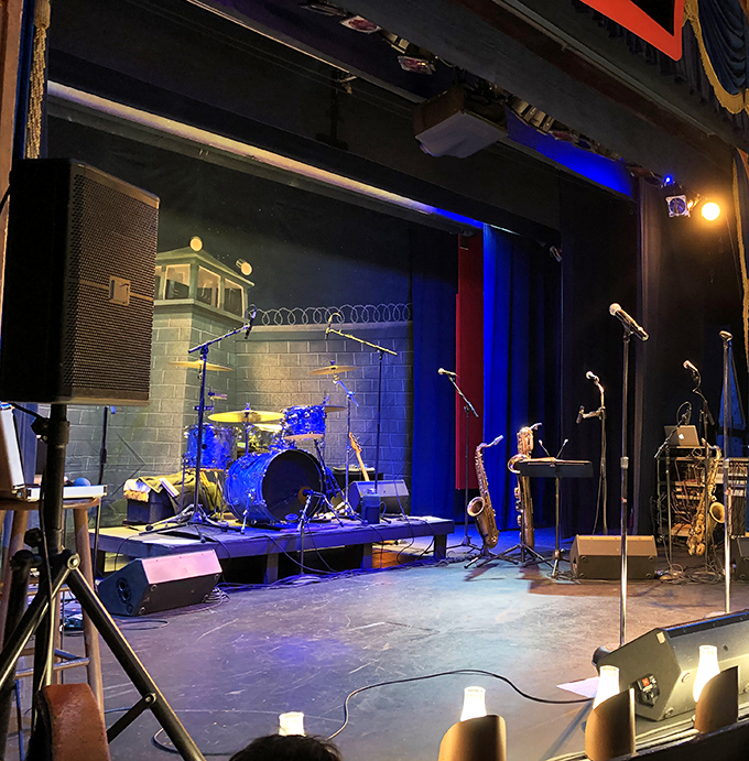 The stage awaits its performers, instruments at the ready. Where burgers come with a side of live music and theatrical flair.