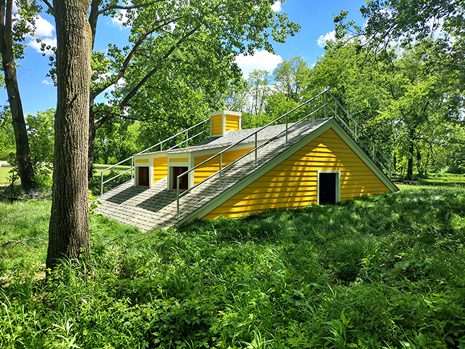 The sunshine-yellow "Oracle of Intimation" emerges from the earth like a geometric submarine, half-buried in a sea of green grass.