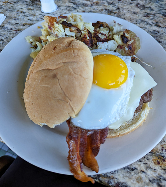 The breakfast burger—where morning meets afternoon in perfect harmony, with a sunny-side-up egg playing referee between bacon and beef.
