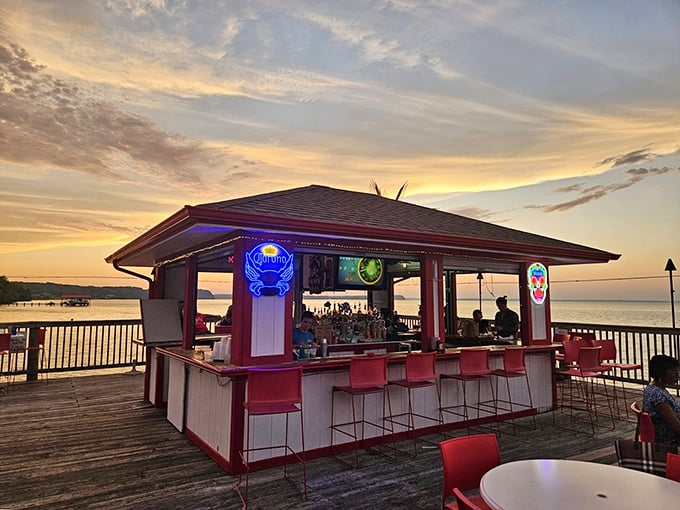 Sunset transforms the outdoor bar into a postcard-worthy scene. Red stools, neon signs, and Potomac views create cocktail hour magic.