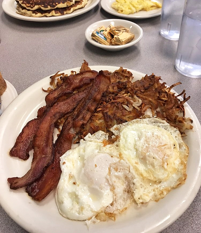 The classic American breakfast trinity: crispy bacon, perfectly fried eggs, and hash browns that crackle with each forkful.