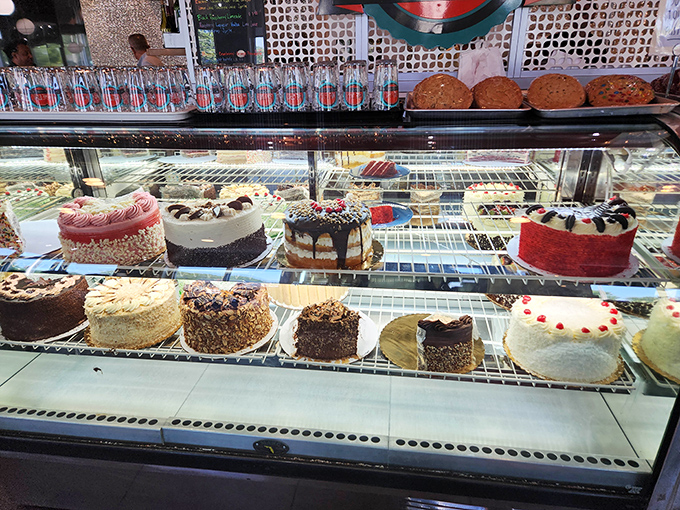 The cake display case—a museum of edible art where willpower goes to surrender and diet plans file for divorce.