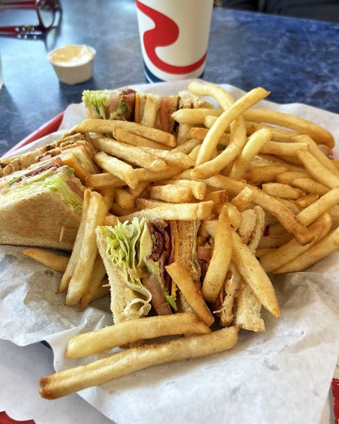 A club sandwich that stands tall and proud, layered with fresh ingredients and surrounded by fries that practically dare you not to finish them.