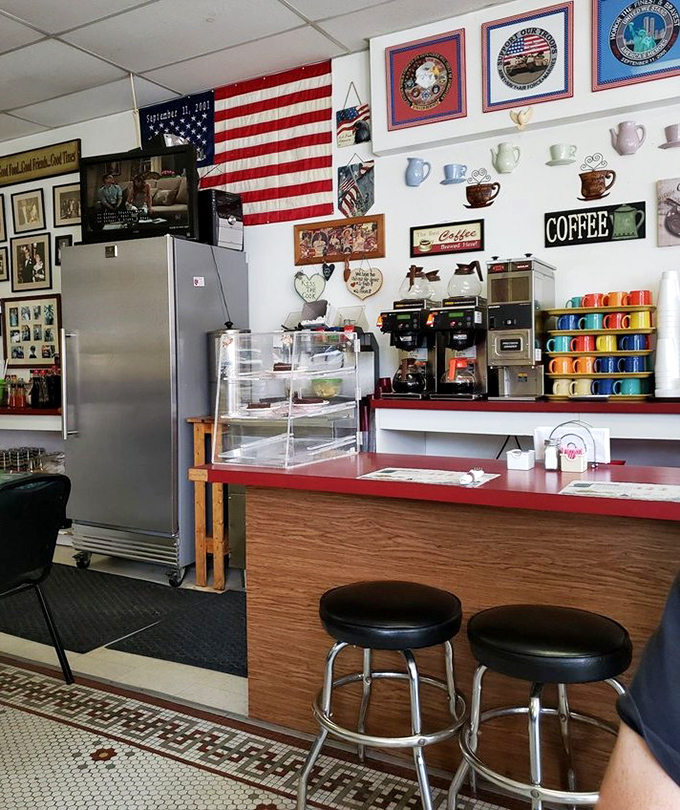 The counter where coffee dreams come true. American flags, memorabilia, and colorful mugs create the backdrop for morning rituals and friendly conversation.