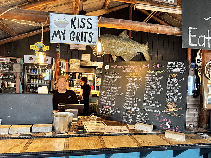 "Kiss My Grits" sign hanging above a smiling face&mdash;the universal symbol for "you're about to eat something unforgettably delicious."