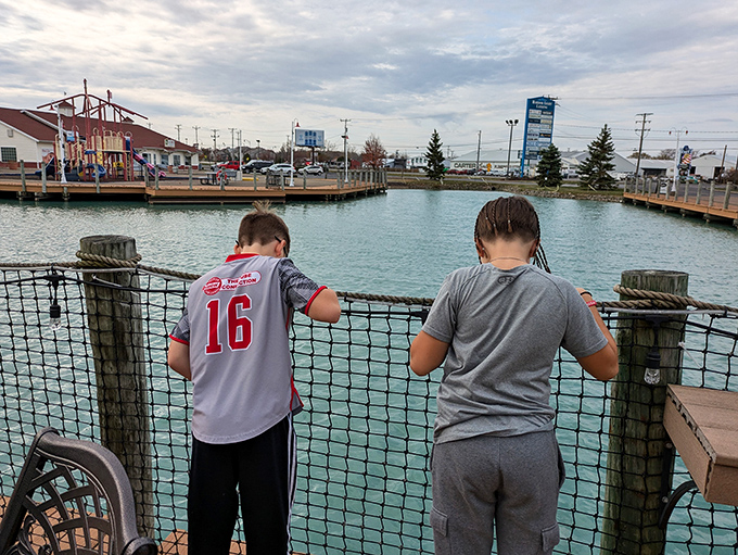 Young visitors lean against the railing, perhaps contemplating which shop deserves their allowance money or just enjoying the marina views.