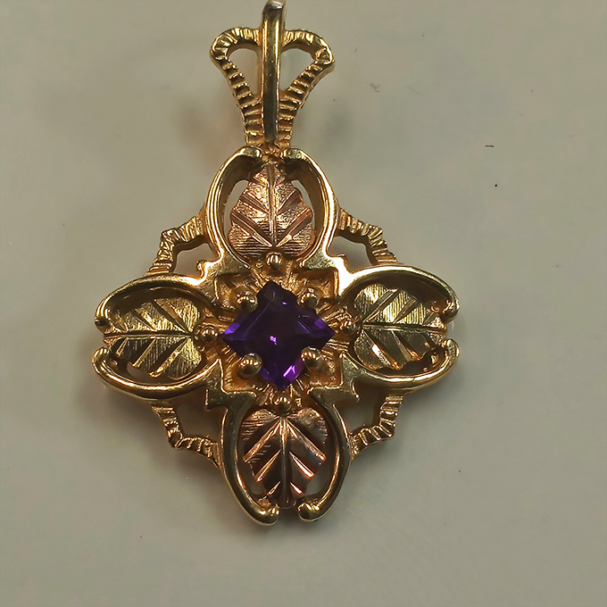 This golden pendant with its purple gemstone center isn't just jewelry; it's wearable art with a story all its own.