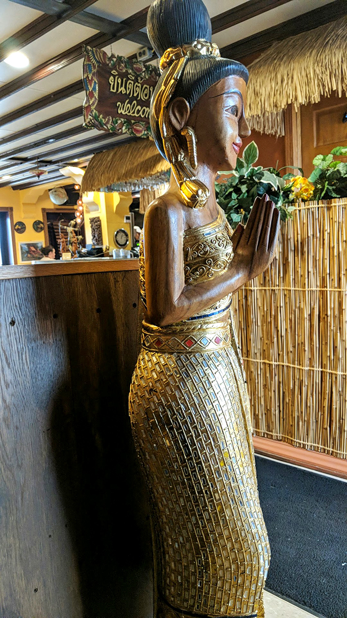 This traditional Thai statue stands in silent welcome, adorned in gold and offering a graceful wai greeting to hungry visitors.