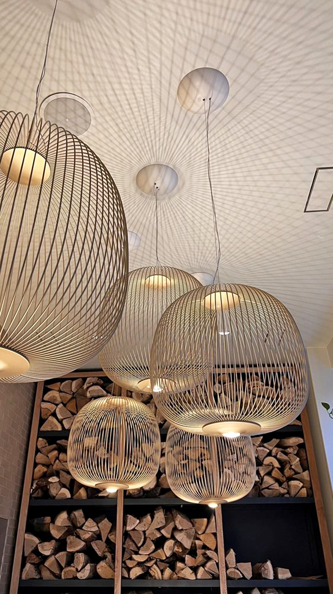 The lighting fixtures float like elegant jellyfish above stacked firewood. This thoughtful design detail speaks volumes about Kann's commitment to both form and flame.