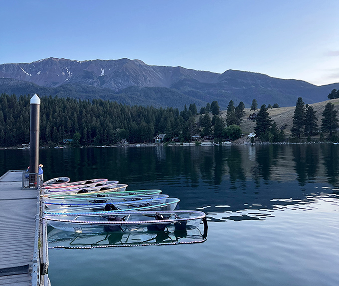 Wallowa Lake's glass surface mirrors mountains while colorful kayaks wait patiently for adventure-seekers. Morning tranquility at its finest.