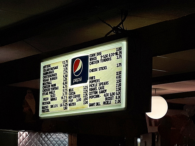 The illuminated menu board&mdash;a beacon of affordable indulgence where funnel cakes and pickle spears share equal billing with cinema classics.