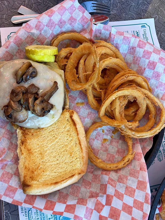 A burger that demands a two-handed commitment, nestled alongside onion rings that form golden halos of crispy perfection.